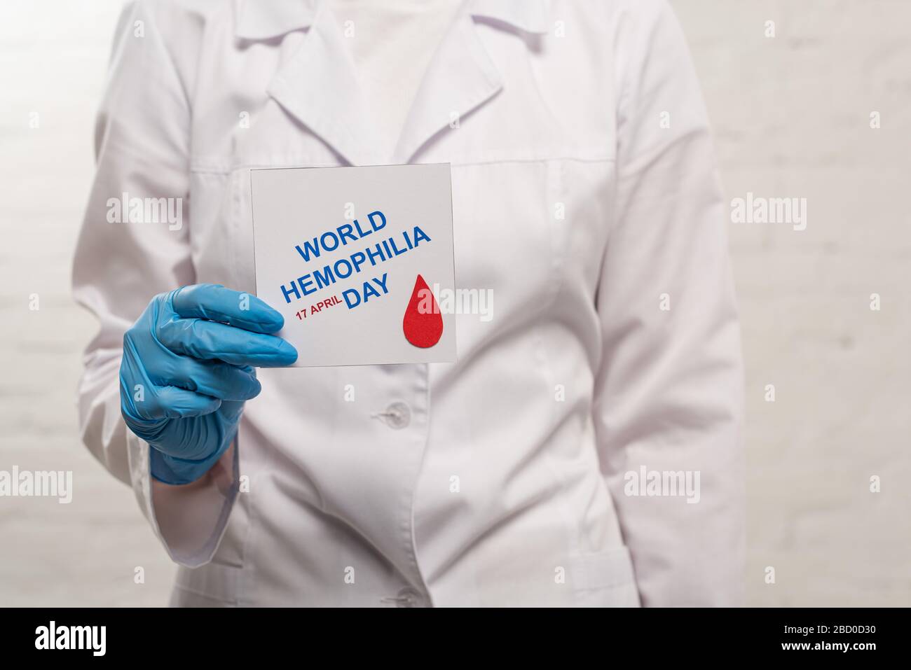 Cropped view of doctor holding card with world hemophilia day on white ...