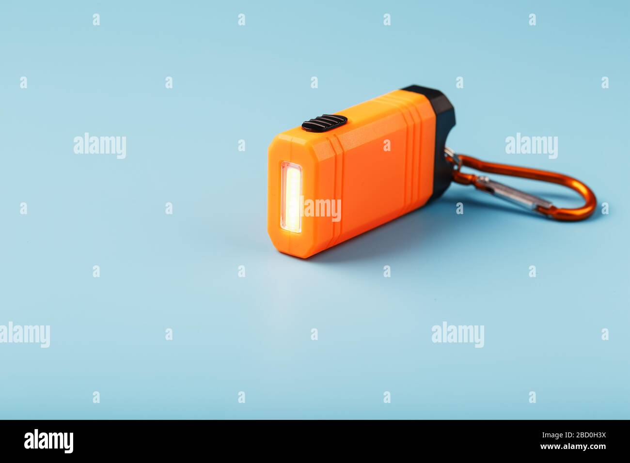 An orange led flashlight with a carabiner glows on a blue background ...