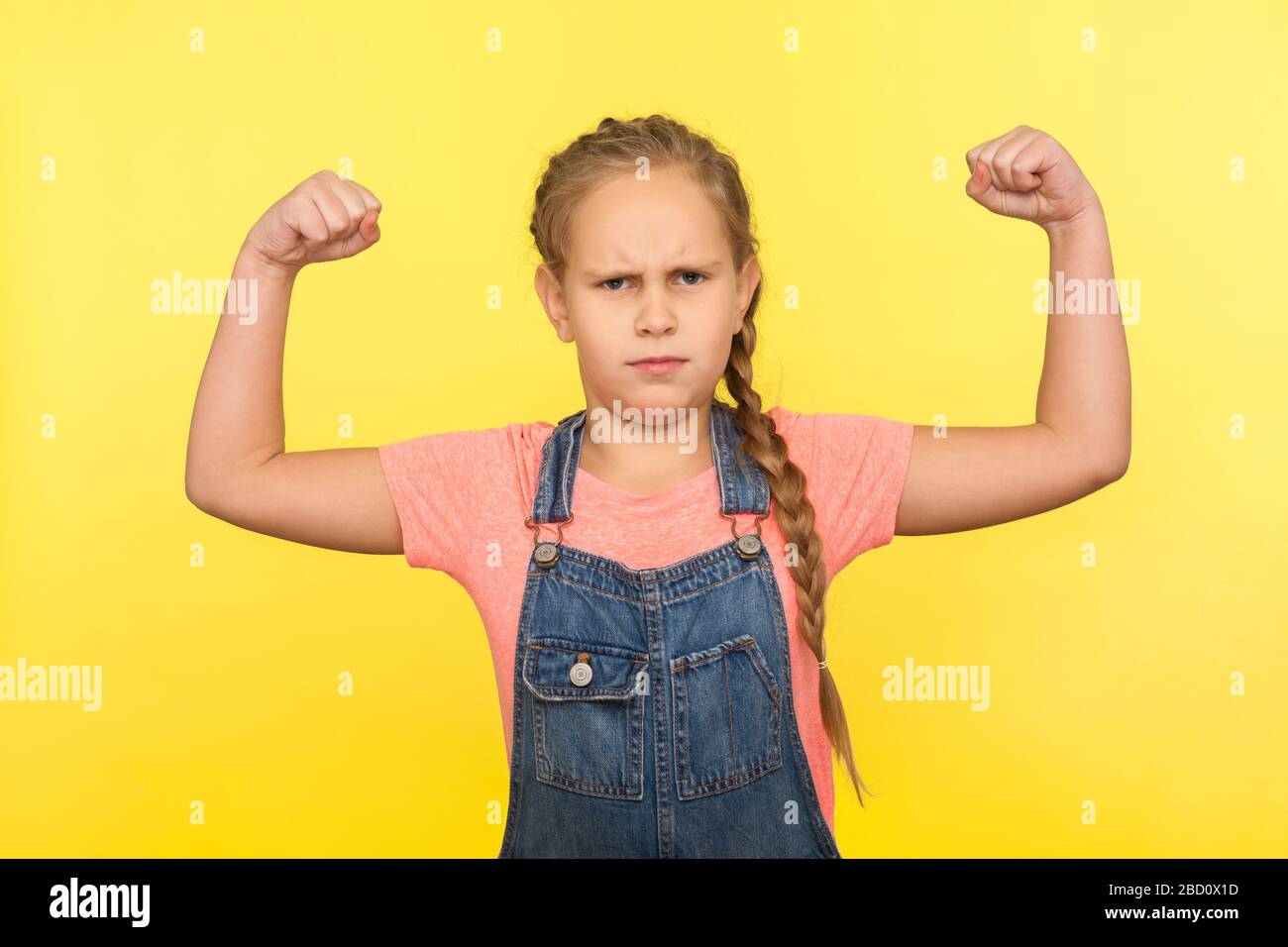 I'm strong! Portrait of brave little girl with braid in denim overalls ...