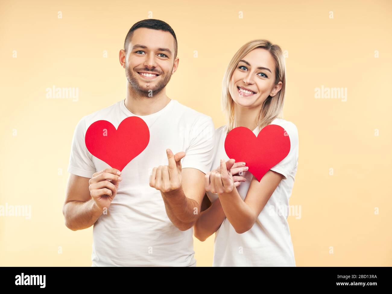 Young couple in love holding big paper hearts in hands over studio ...