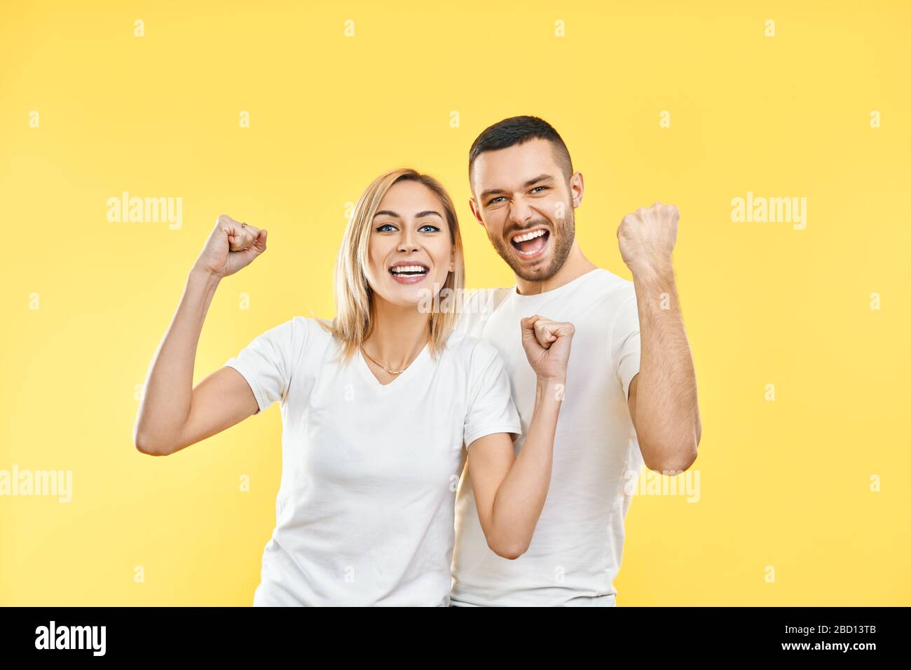 Happy couple celebrating success with winner gesture on yellow ...