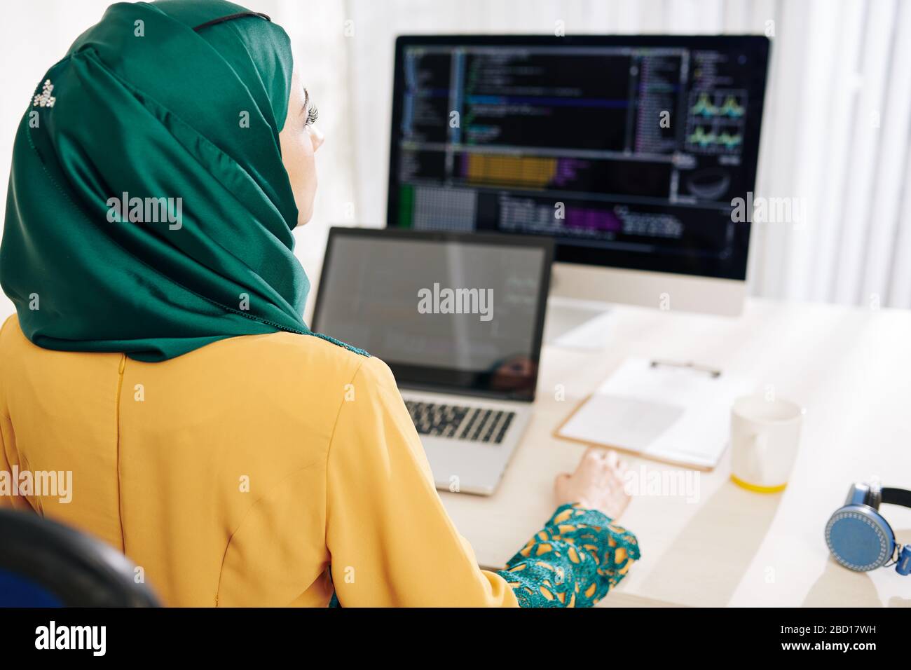 Young female muslim code in beautiful emerald hijab working on computer ...