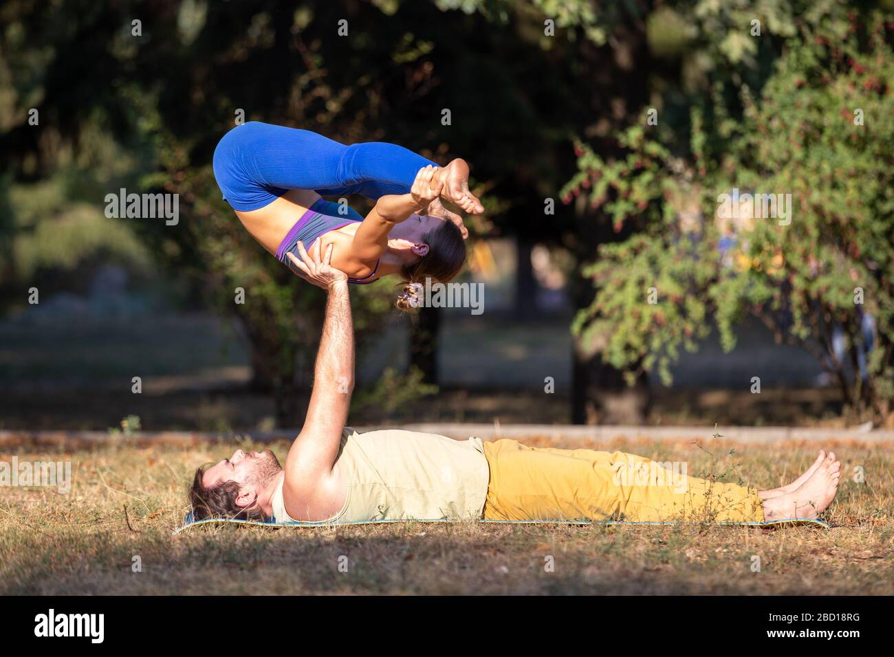 Young couple doing acroyoga exercises in park. Man holding woman on ...
