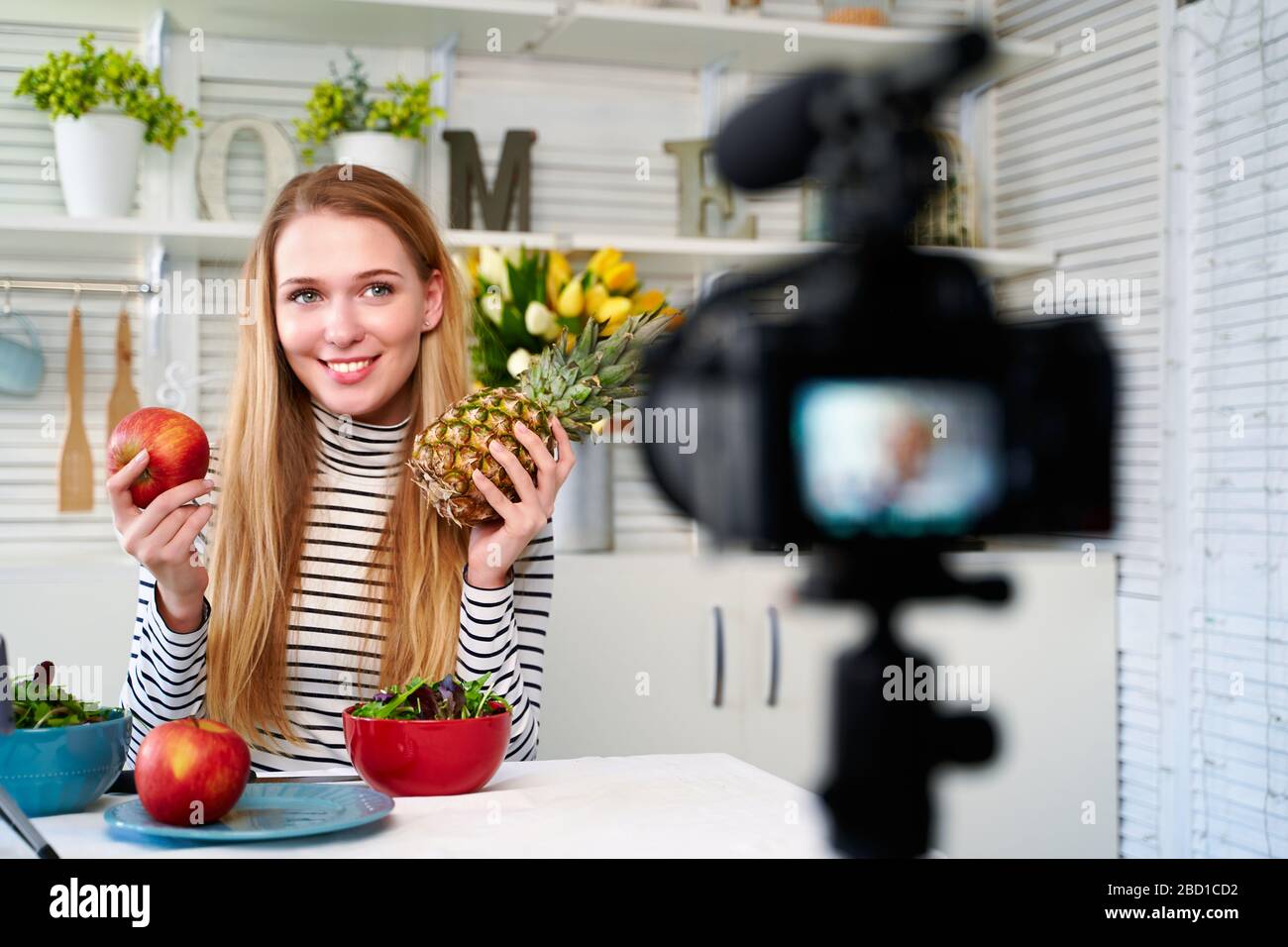 Food blogger cooking fresh vegan salad of fruits in kitchen studio ...
