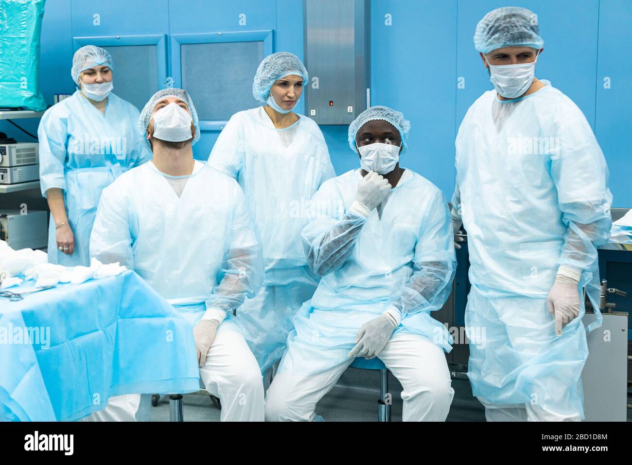 A team of doctors in uniform and medical masks rests after completion ...