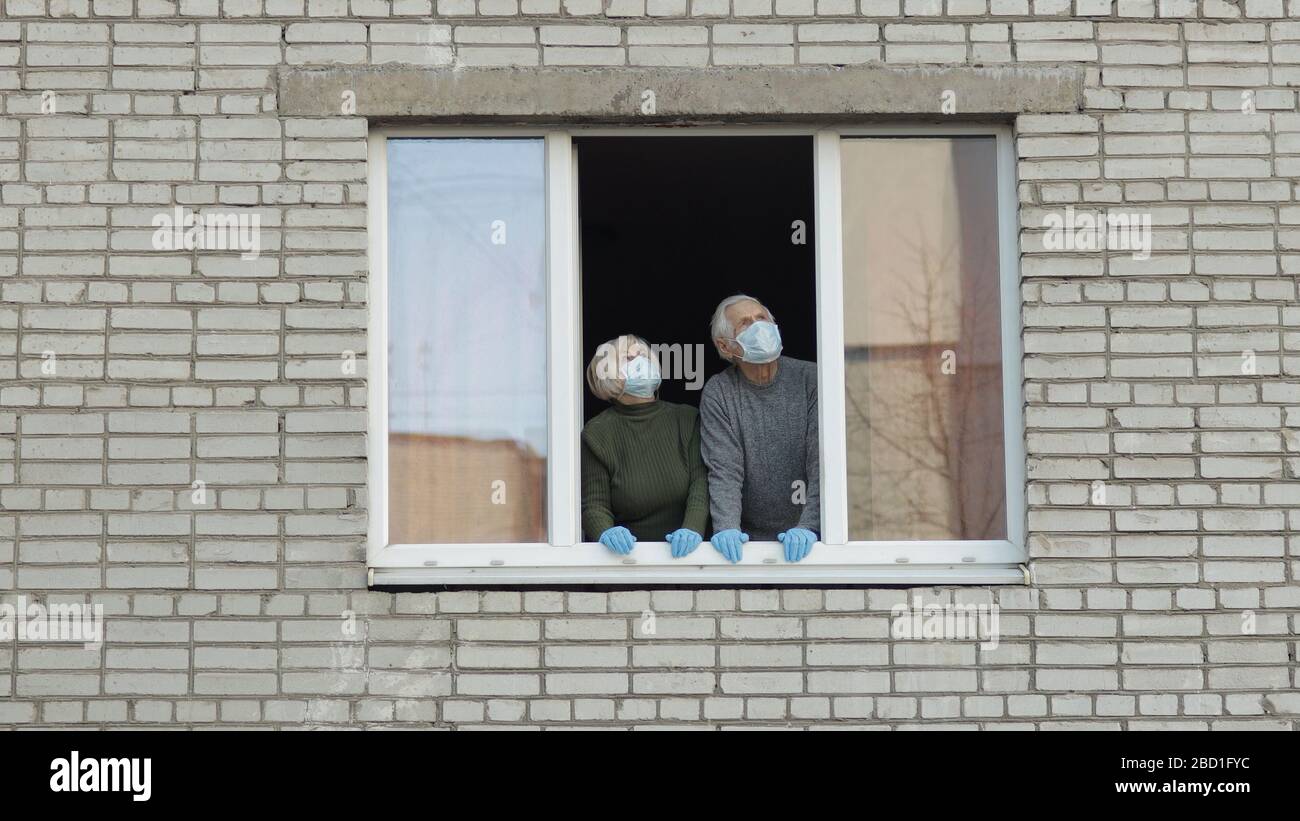 Old grandfather and grandmother at window in protection mask. Isolated ...