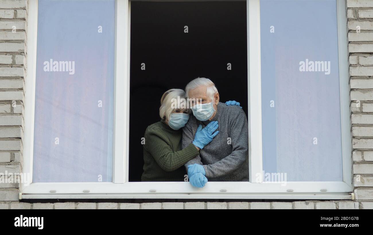 Old grandfather and grandmother at window in protection mask. Isolated ...