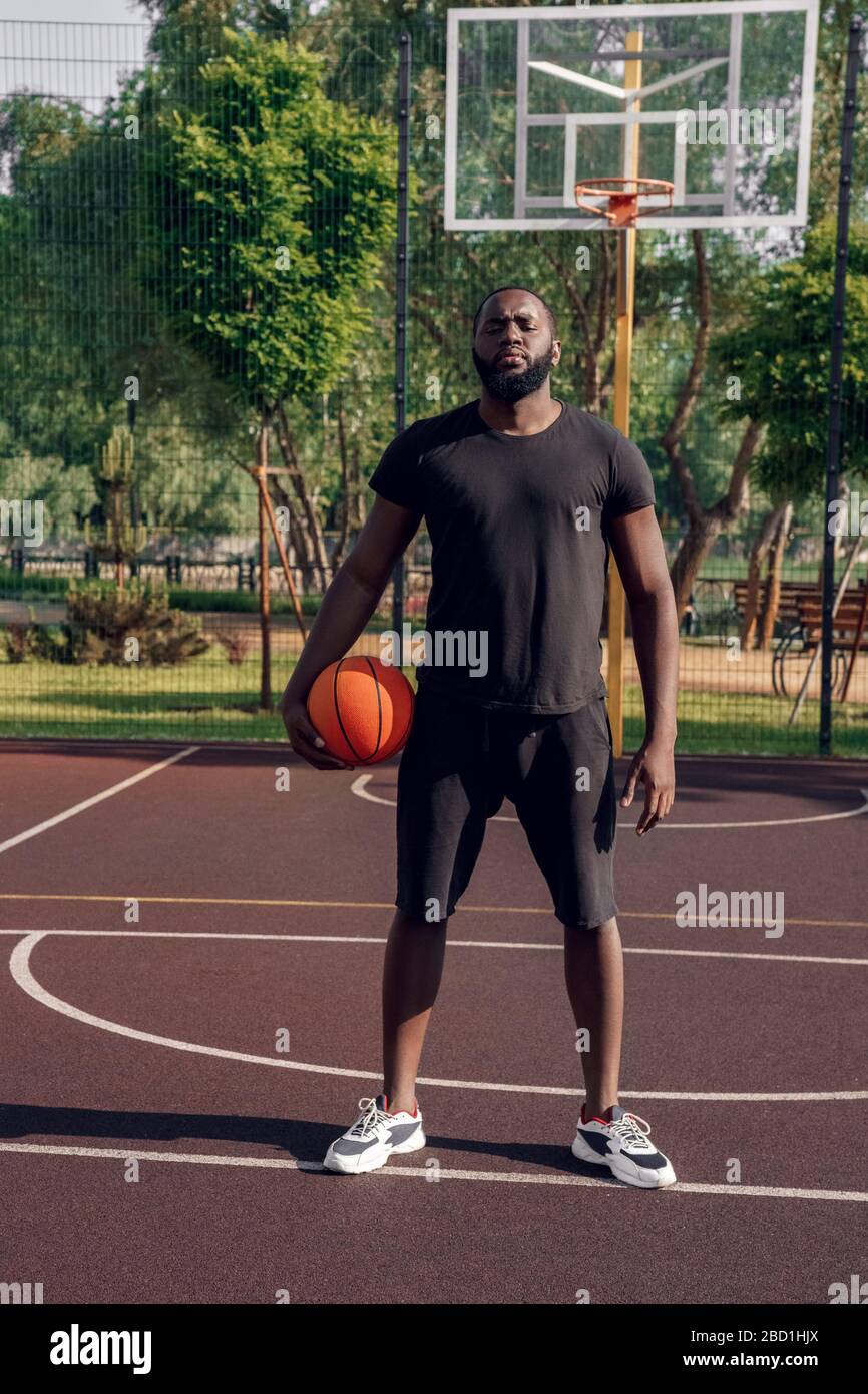 Outdoors Activity. African man standing with ball on basketball court ...