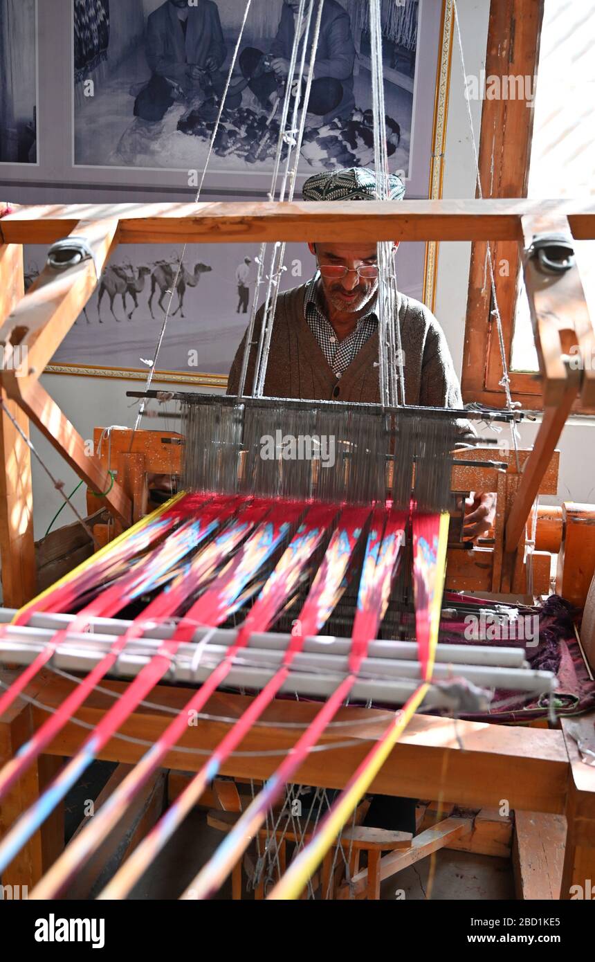 Uyghur man at loom weaving tie dyed silk thread into traditional cloth ...