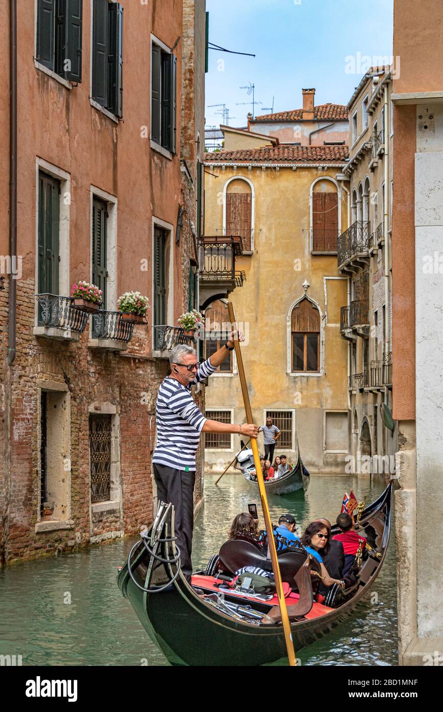 A gondola with tourists looking at the buildings as the Gondolier moves ...