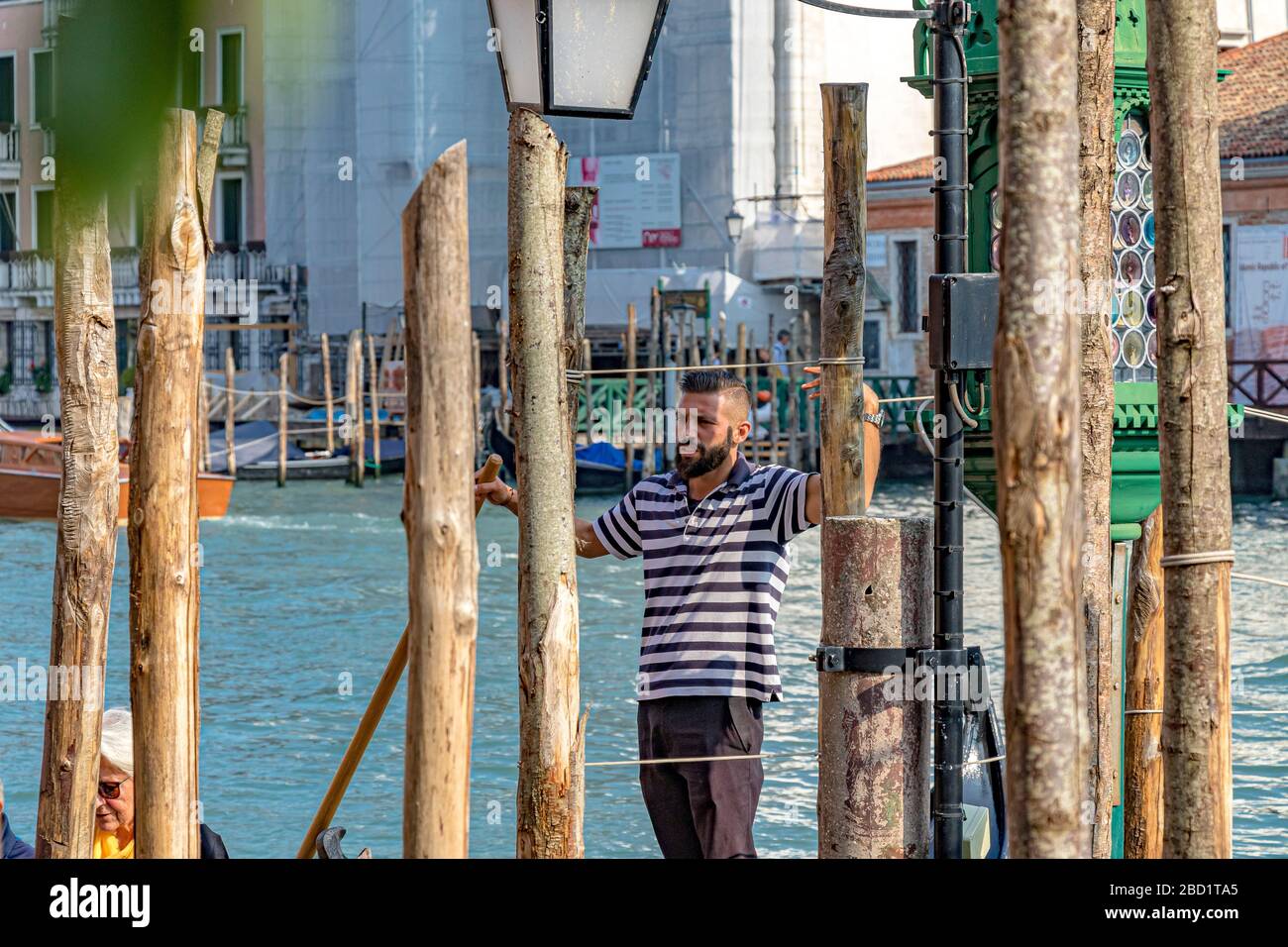 A Gondolier in a striped gondolier shirt standing between wooden ...