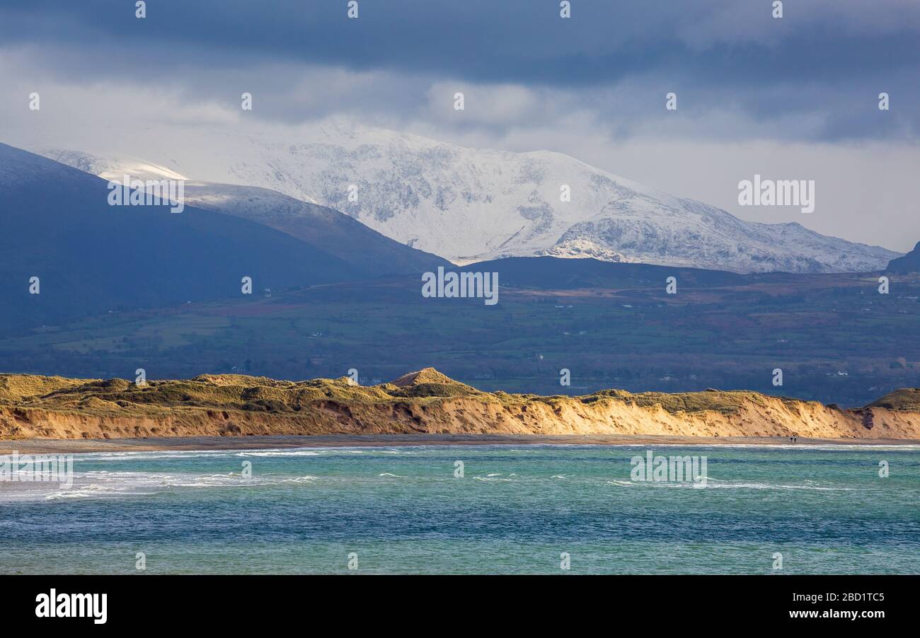 Newborough beach and sand dunes with a snow covered Mount Snowdon in ...