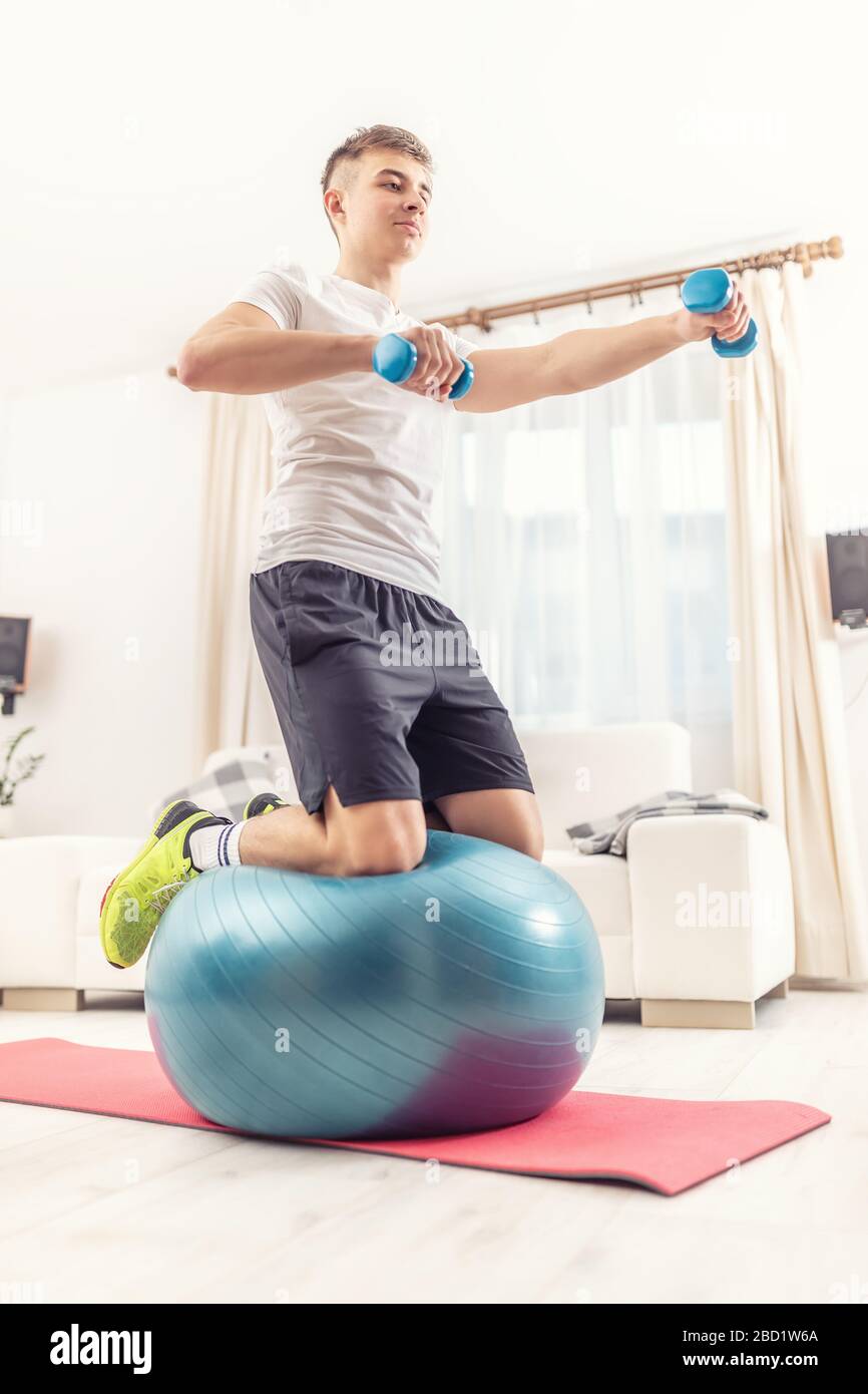 Athletic caucasian young man kneeling on a fitness ball holding upright ...