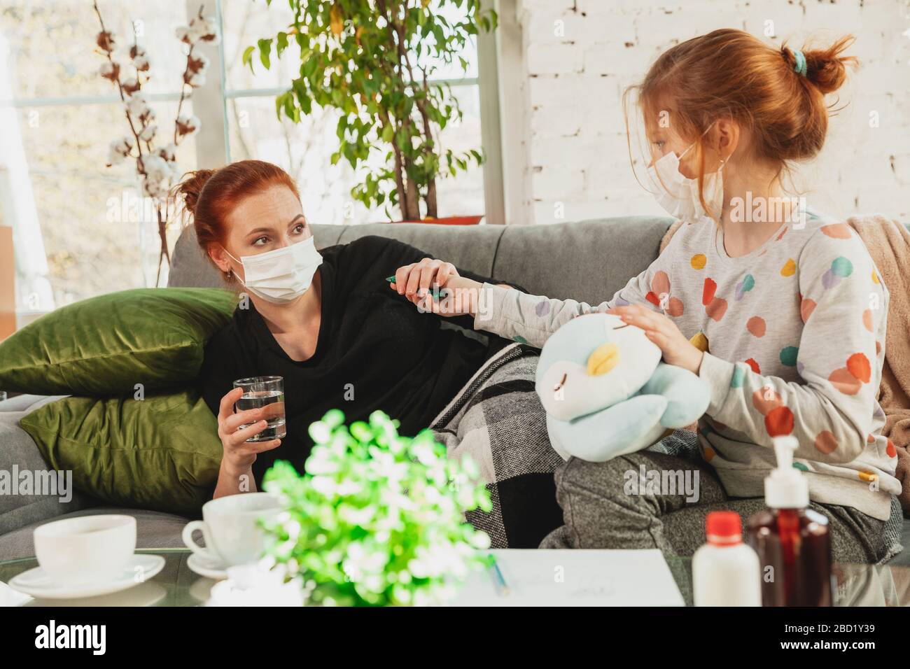 Mother and daughter in face masks and gloves isolated at home with ...