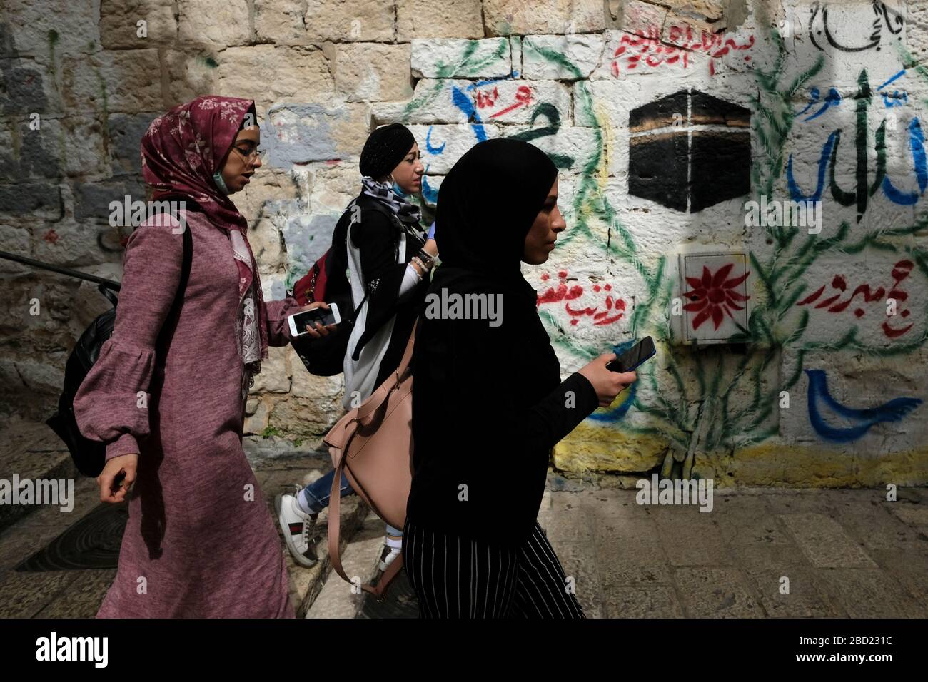 Palestinian women wearing hijab headdress walk past a wall decorated ...