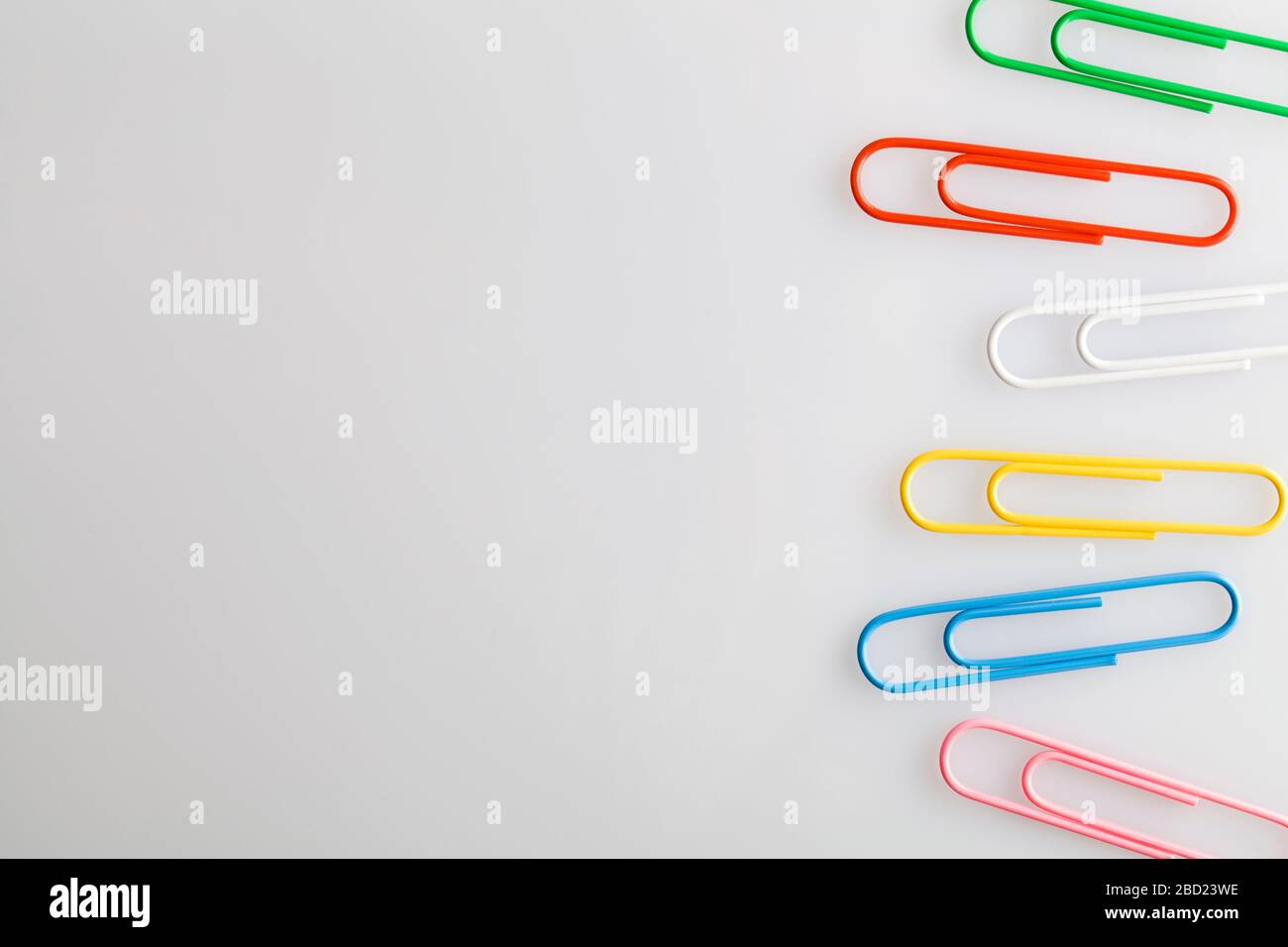 multi colored paper clips on white, gray background. copy space flat ...