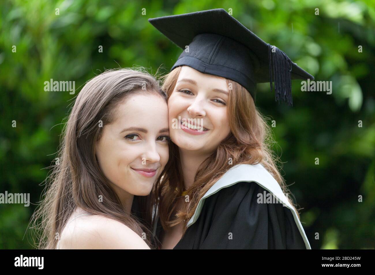Female university graduate posing outdoors with her younger sister ...