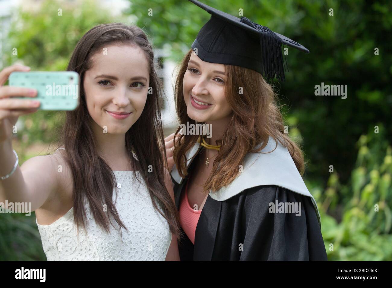 Female university graduate posing outdoors with her younger sister ...