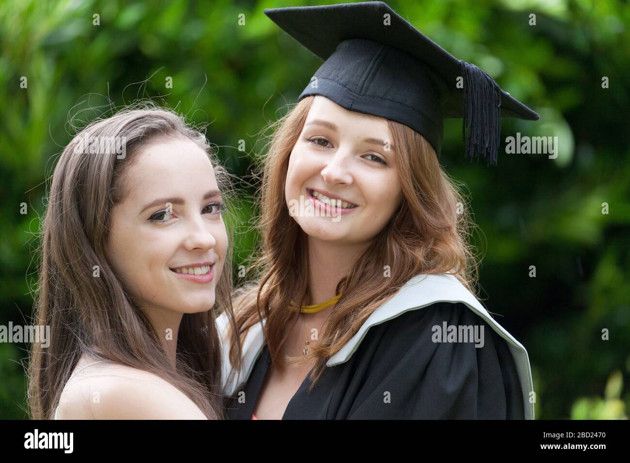 Female university graduate posing outdoors with her younger sister ...