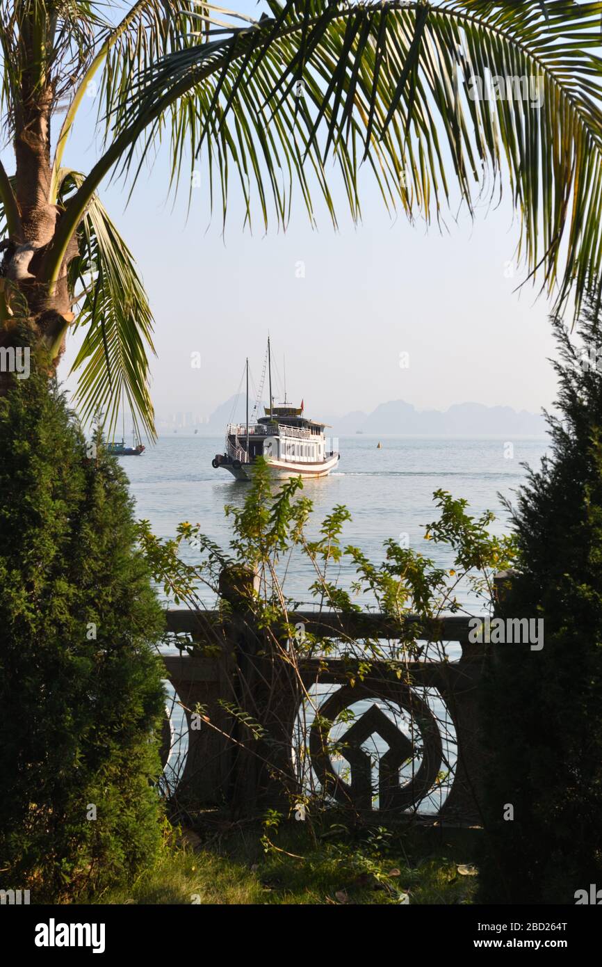 A Chinese junk ferry in UNESCO's renowned Ha Long Bay framed with palm ...