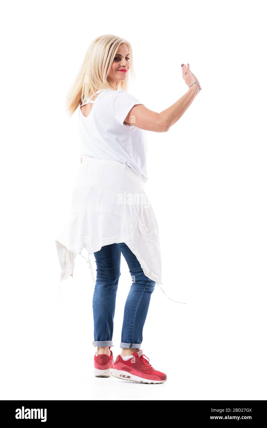 Back view of happy mid age woman walking away turning behind and waving ...