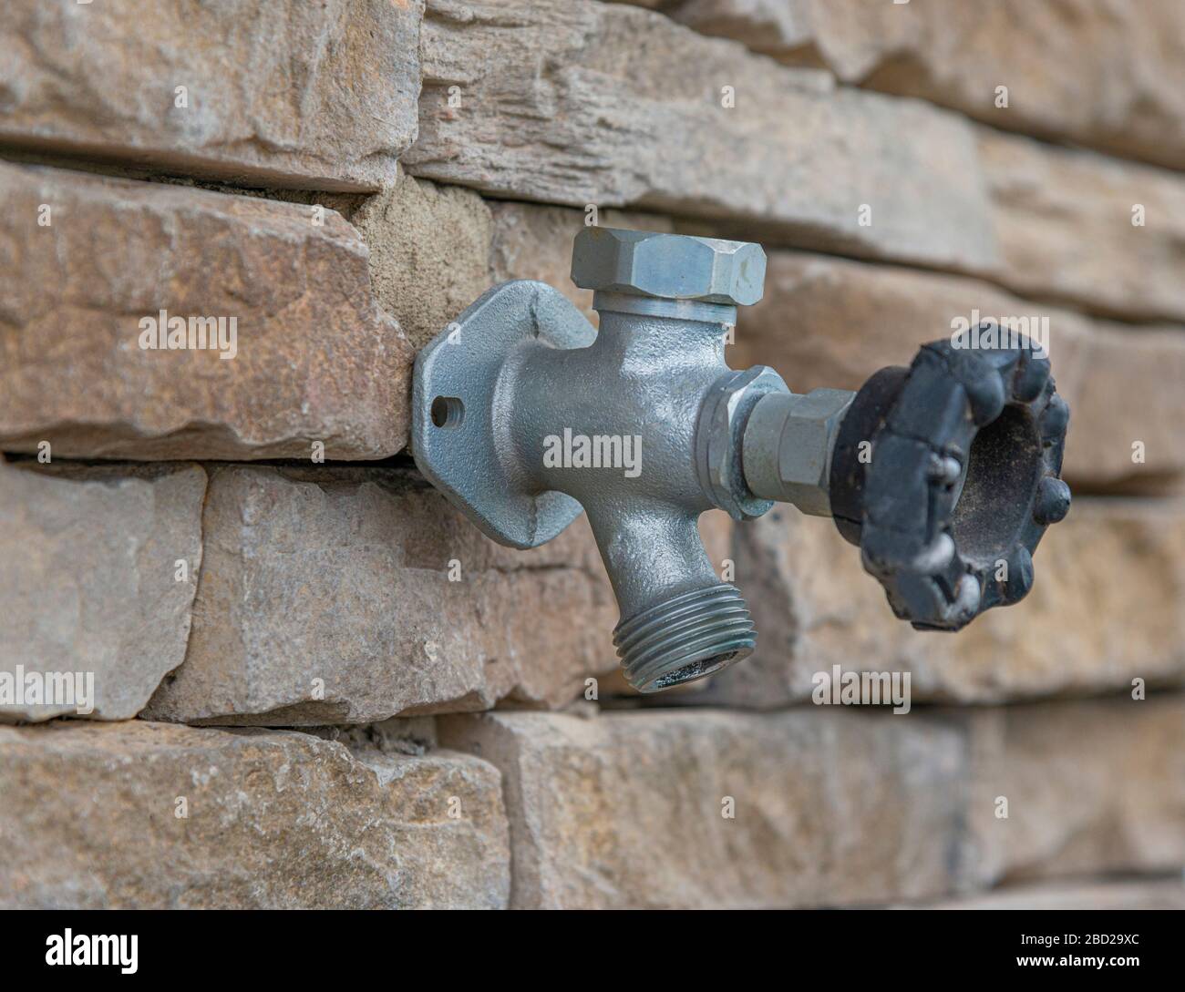 Horizontal close-up shot of an outdoor water faucet attached to a stone ...