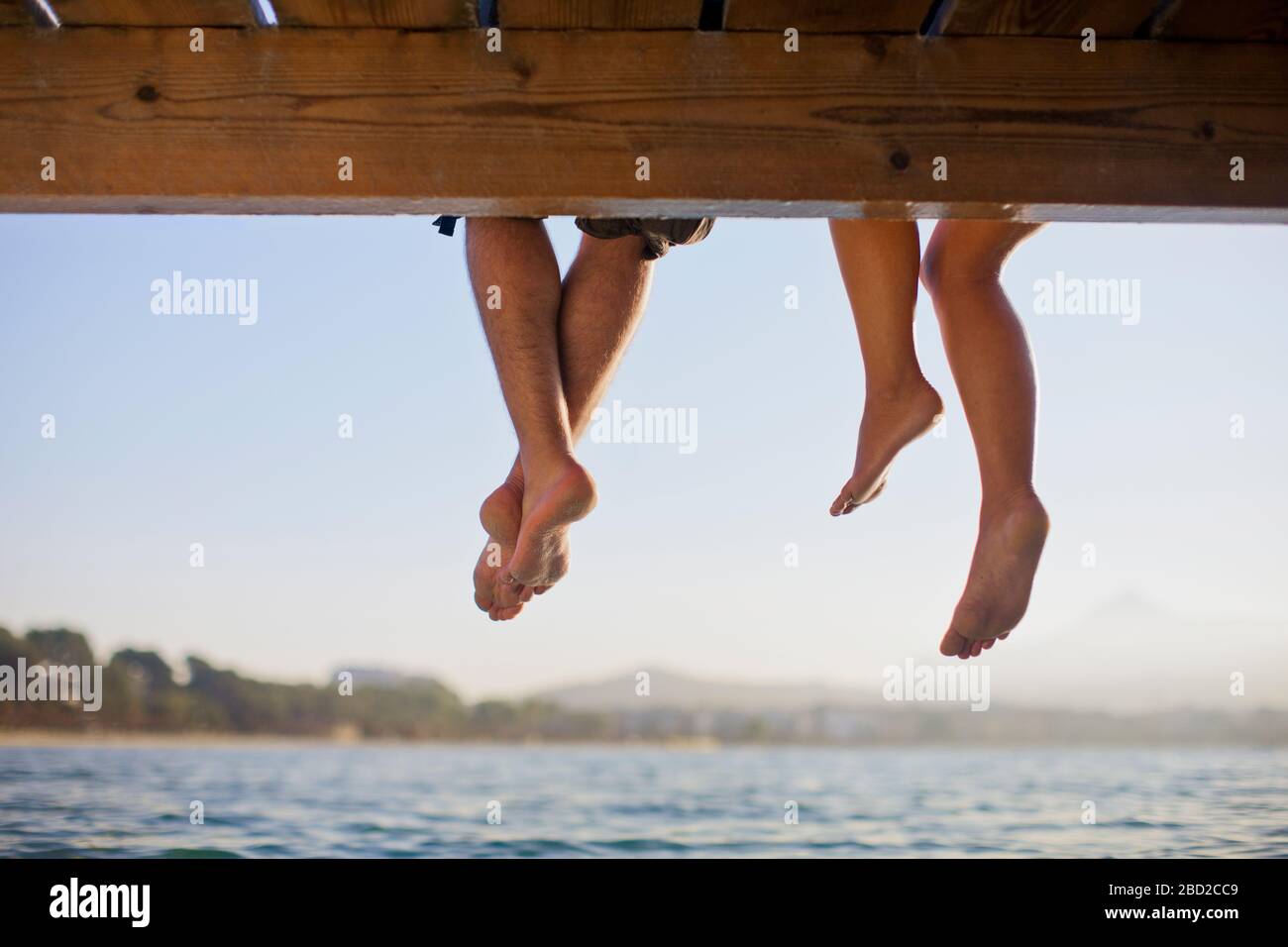 Two pairs of legs dangling off a wooden pier Stock Photo - Alamy