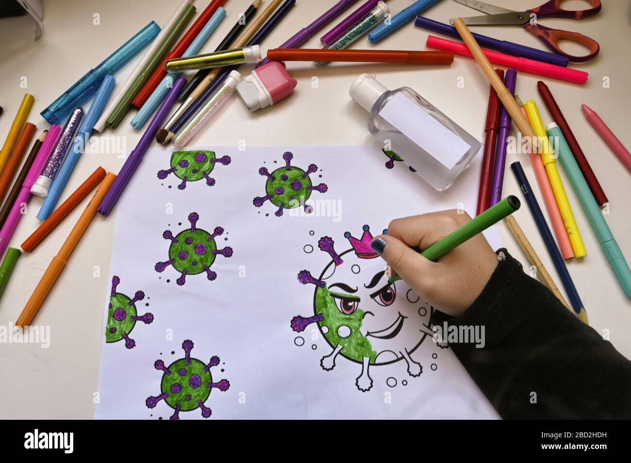 A child coloring virus painting on a table full of colors and a bottle ...