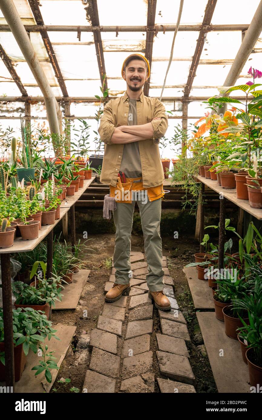 Portrait of cheerful handsome young bearded greenhouse grower with ...