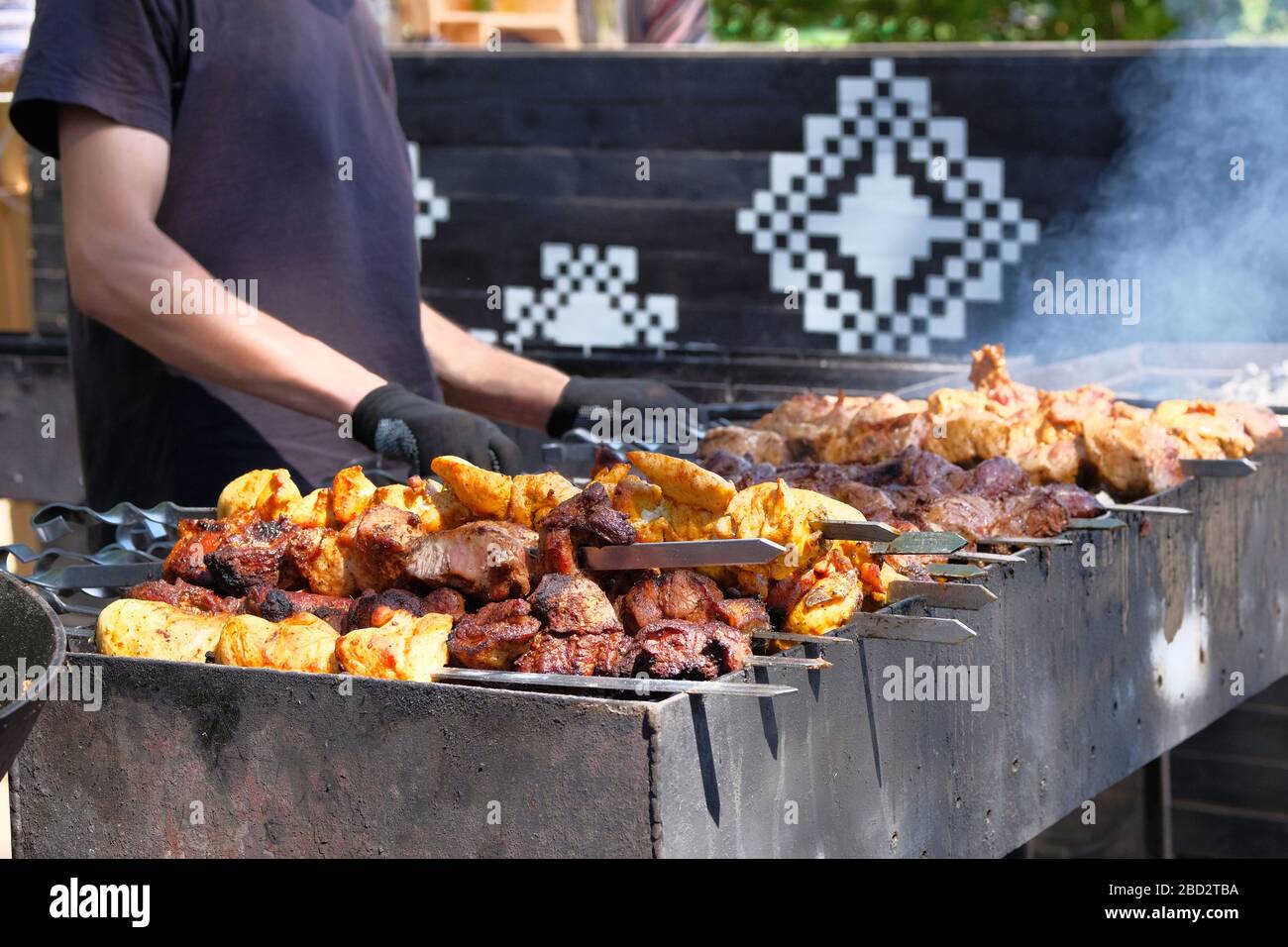 Man in black T-shirt roasting marinated meat on grill. Street food and ...