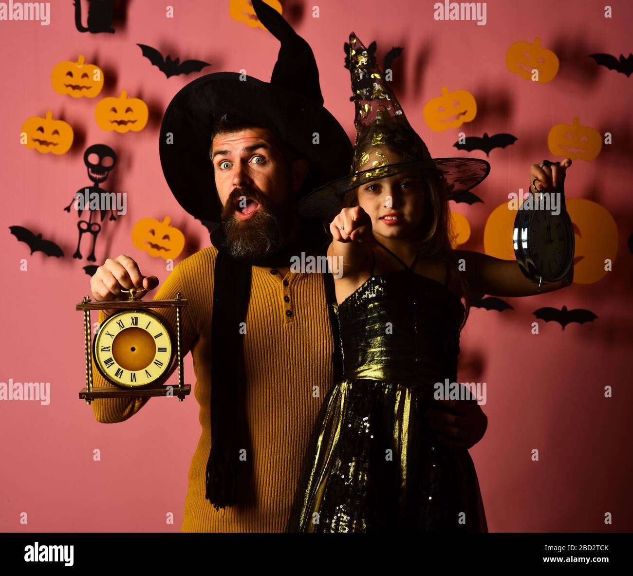 Wizard and little witch in black hats hold old clocks. Halloween party ...