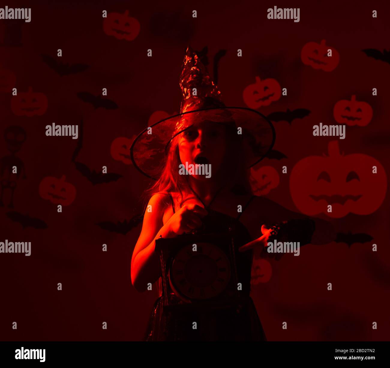 Young girl in witch halloween costume with big old clock and scared ...