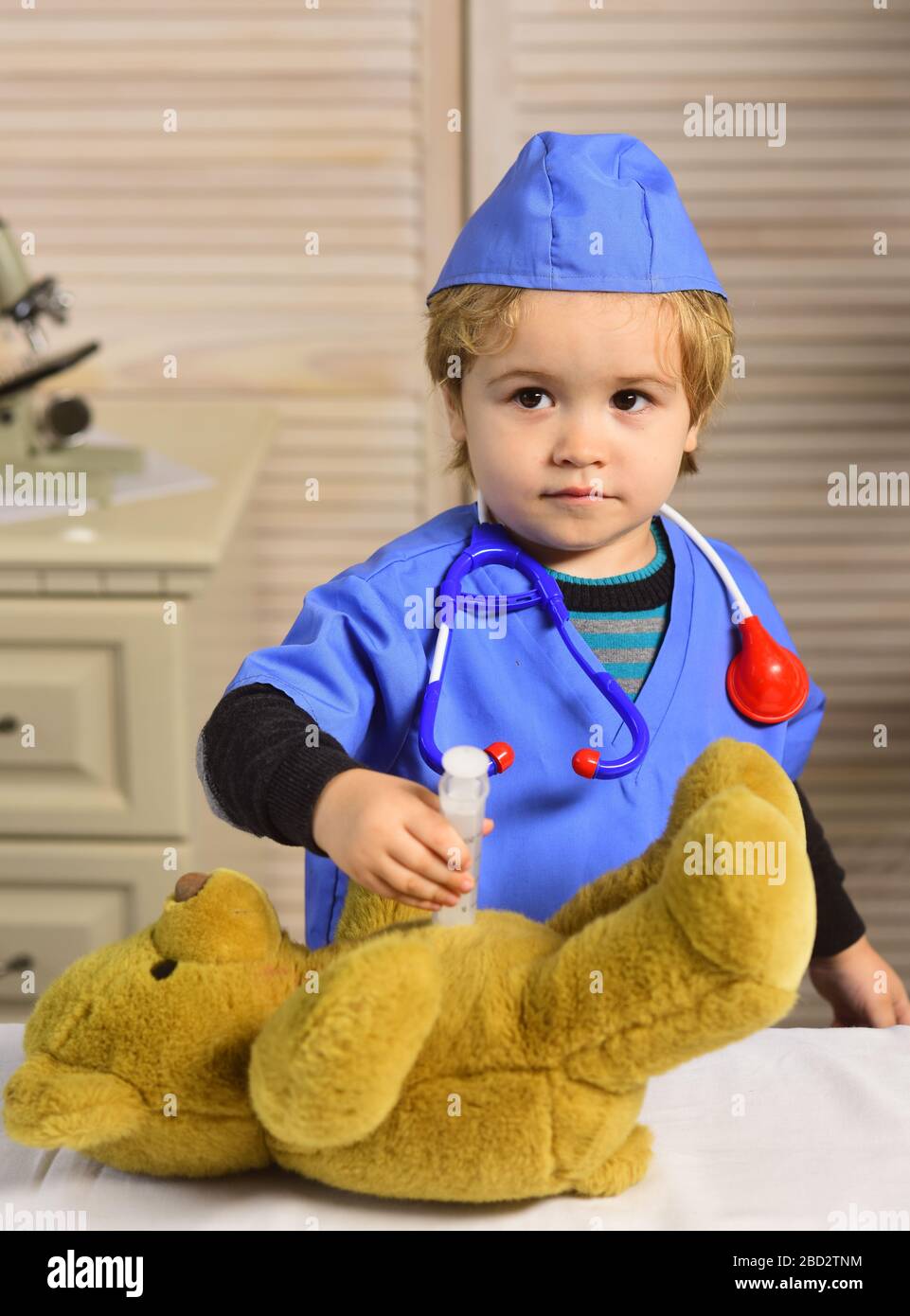 Boy in surgical uniform holds syringe on wooden background. Little vet ...
