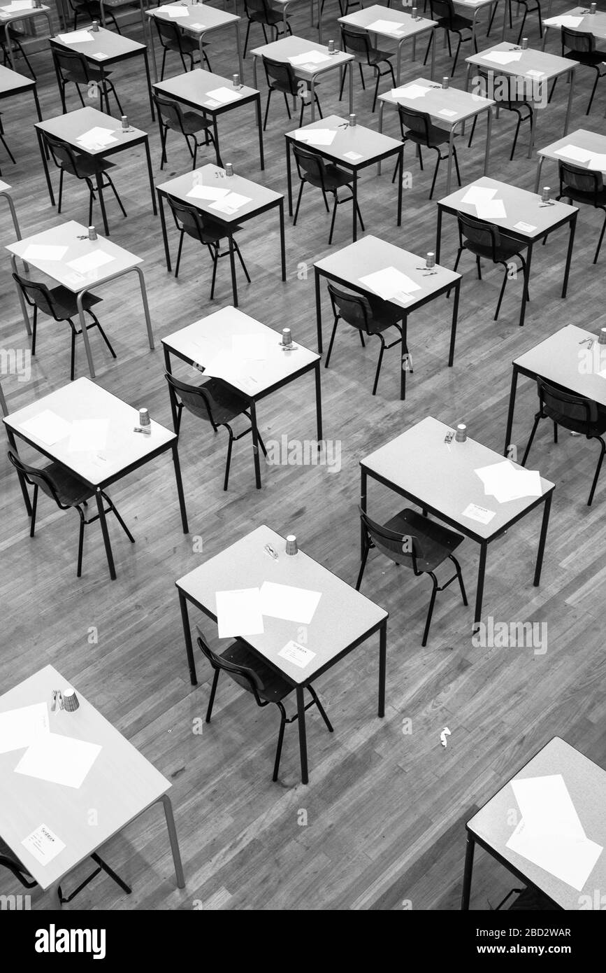 rows of empty tables and chairs in exam room at highschool in black and ...