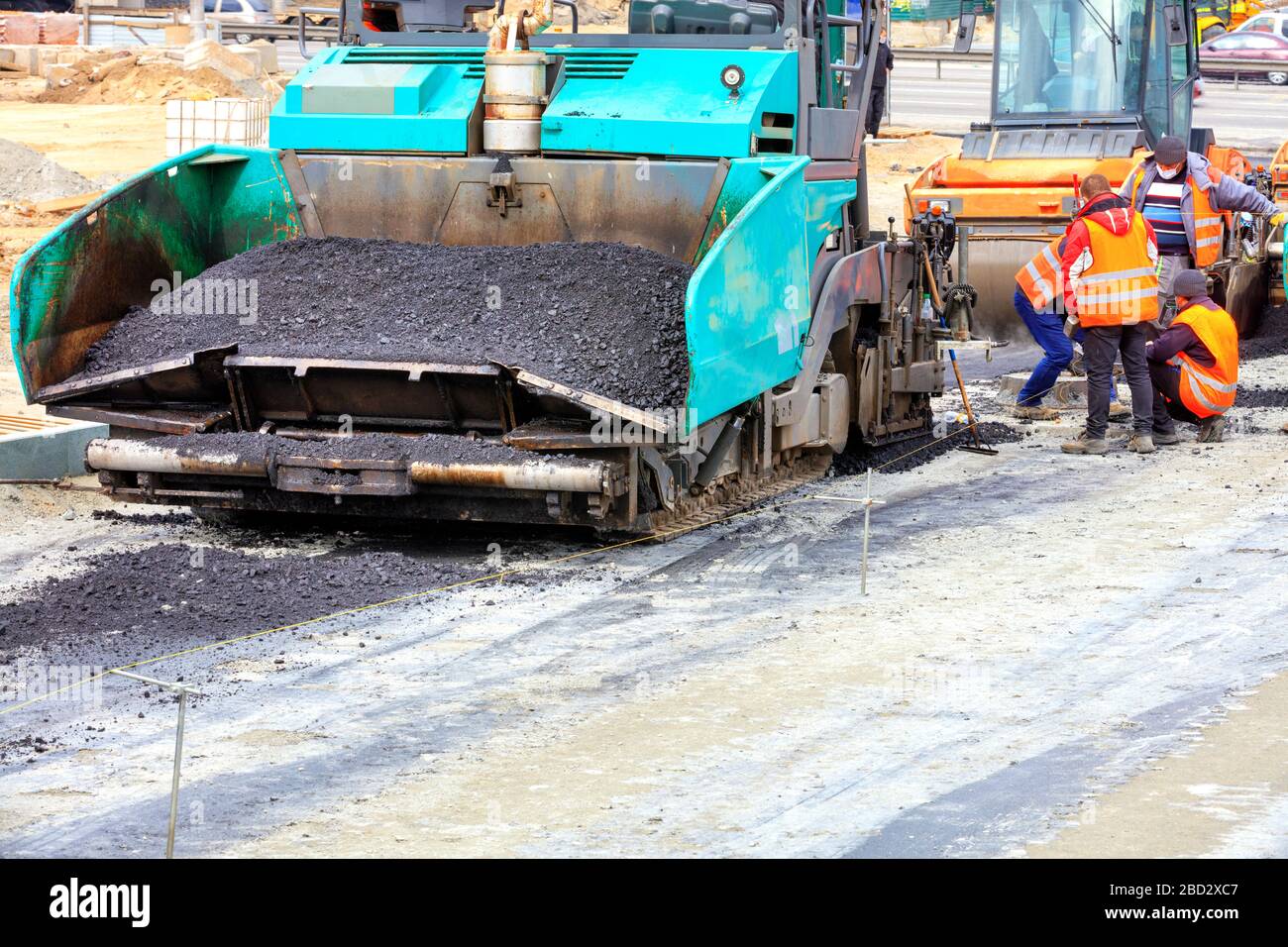 A large asphalt paver and a road vibratory roller go one after another ...