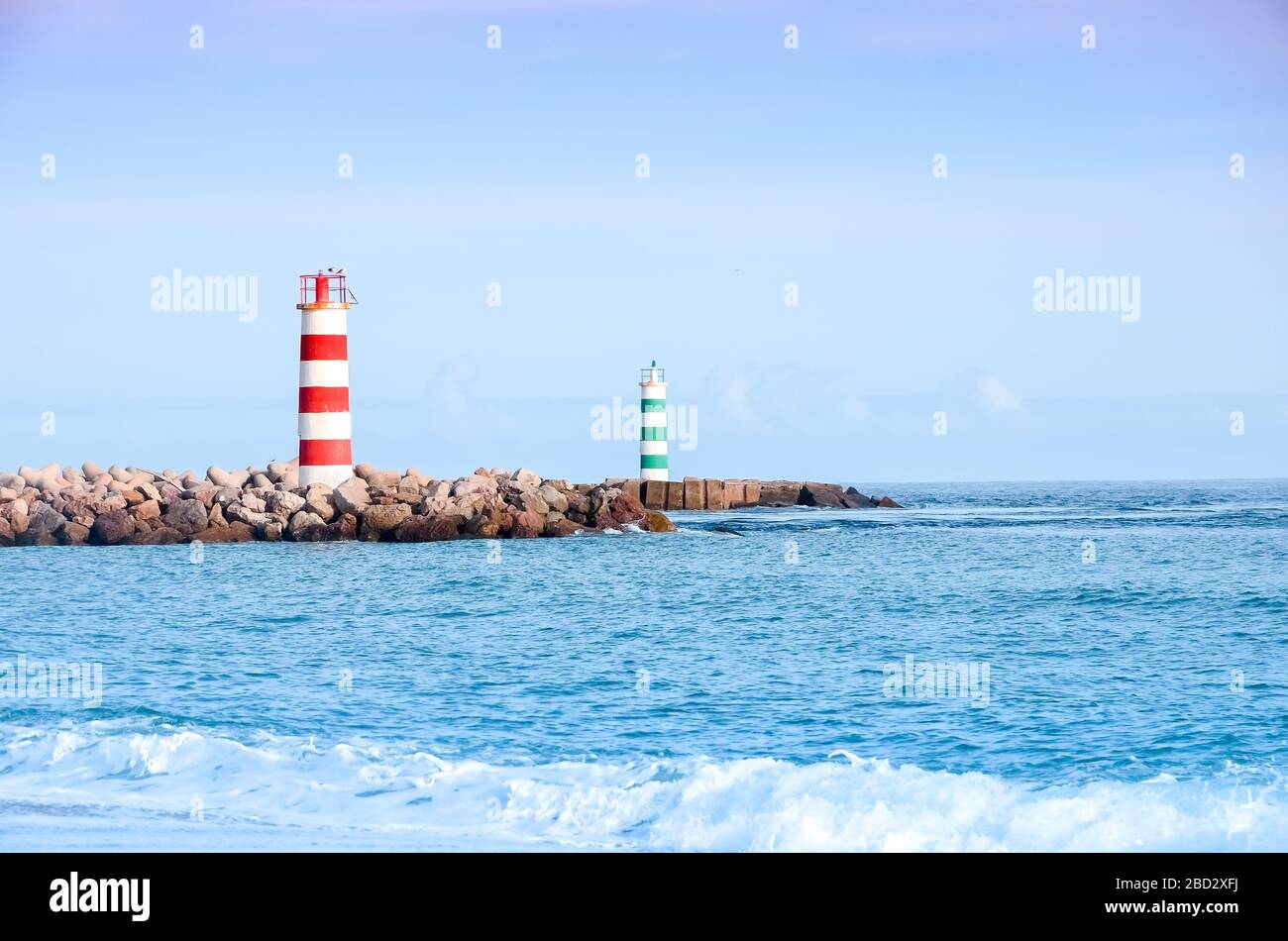 Two striped lighthouses stand on the beach in the city of Faro in ...