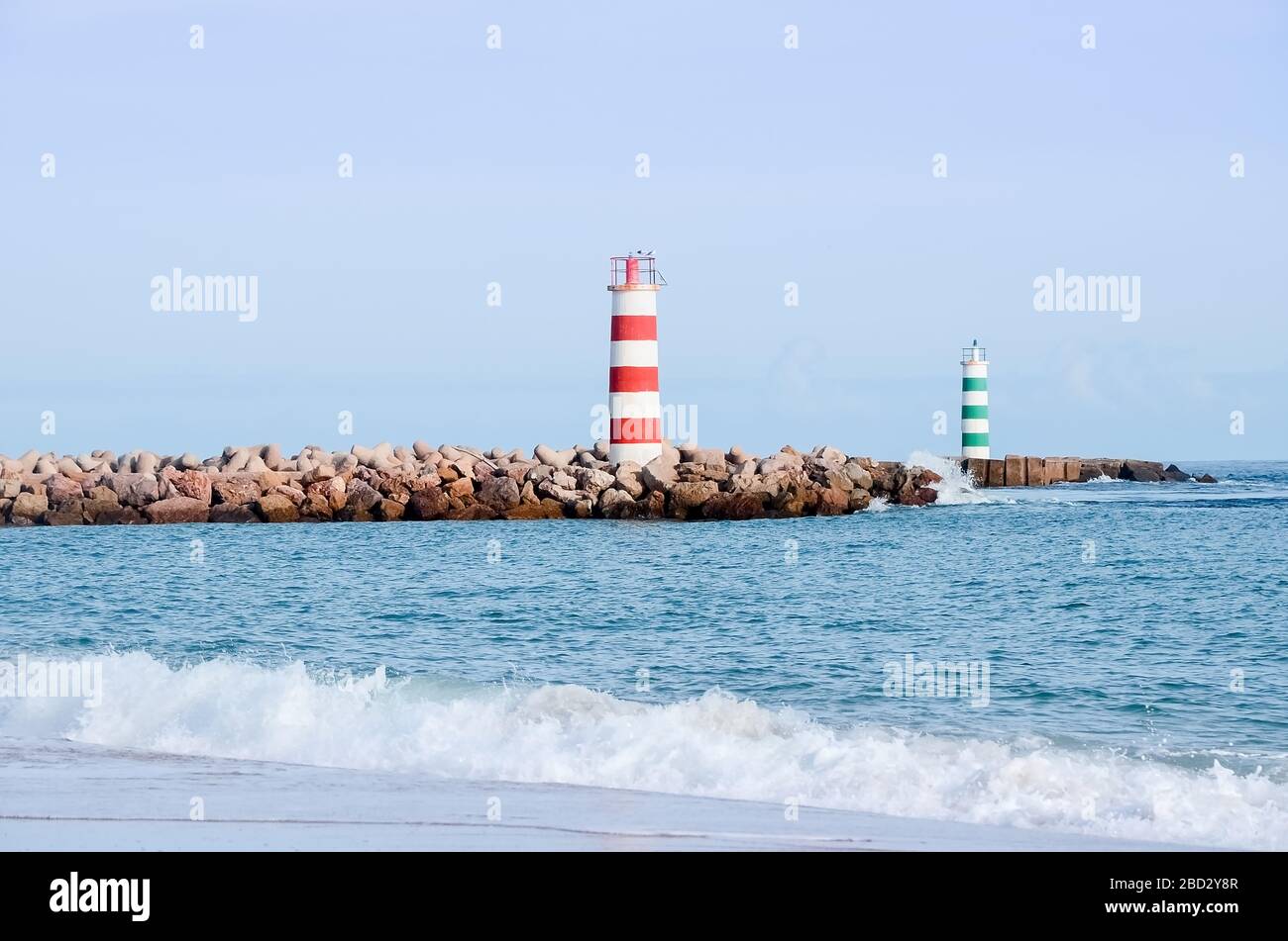 Two striped lighthouses stand on the beach in the city of Faro in ...