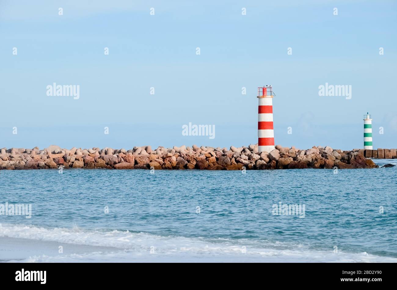 Two striped lighthouses stand on the beach in the city of Faro in ...