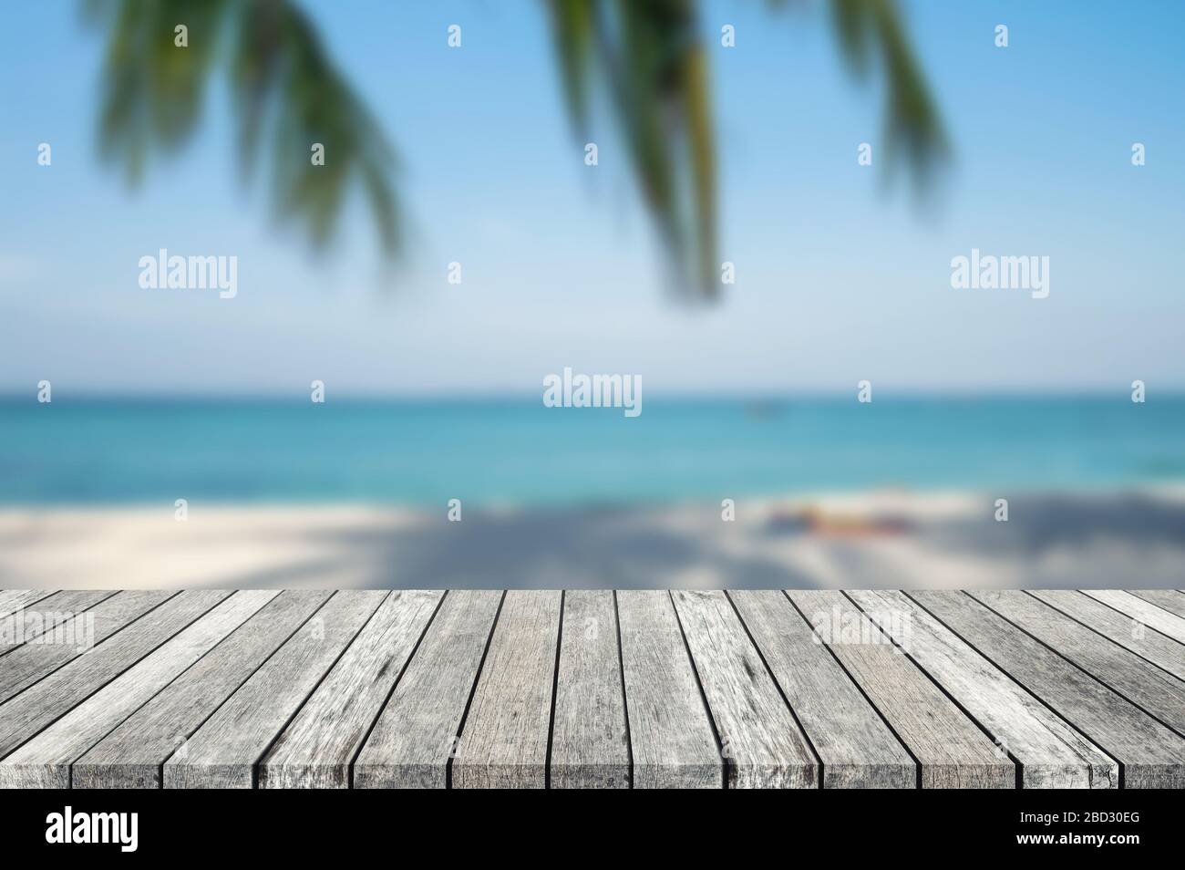 Wooden gray tabletop with blurred scene of tropical beach and plam leaf ...