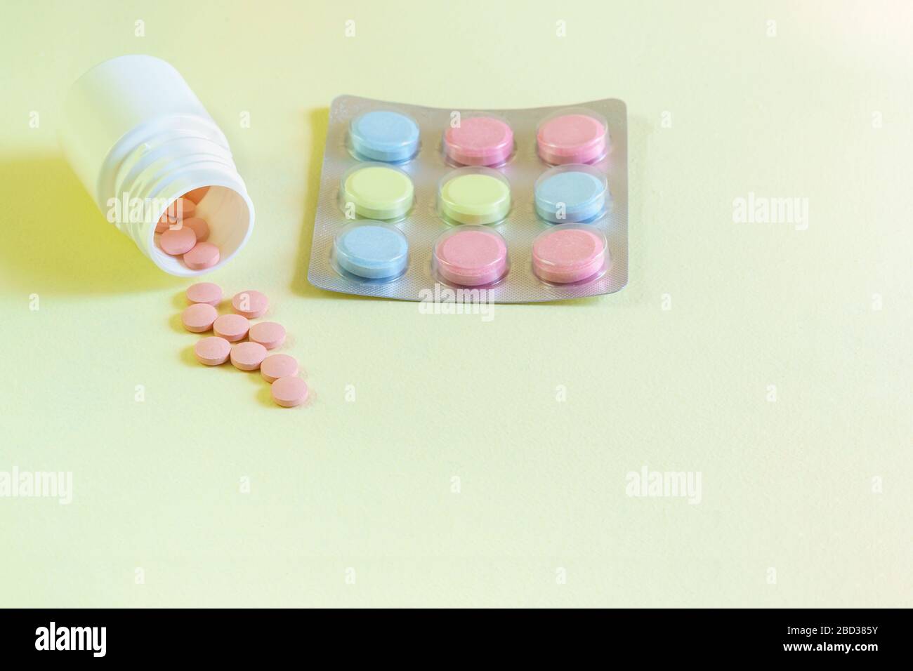 Pink, yellow and blue tablets on a yellow table. Multicolored medicines ...