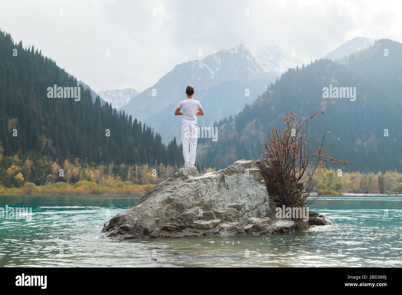 A man in a Samasthiti pose on a stone among a mountain lake Stock Photo ...