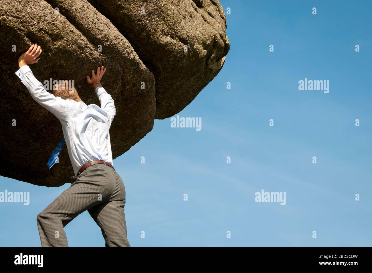 Strong businessman struggling to lift massive boulder into blue sky ...
