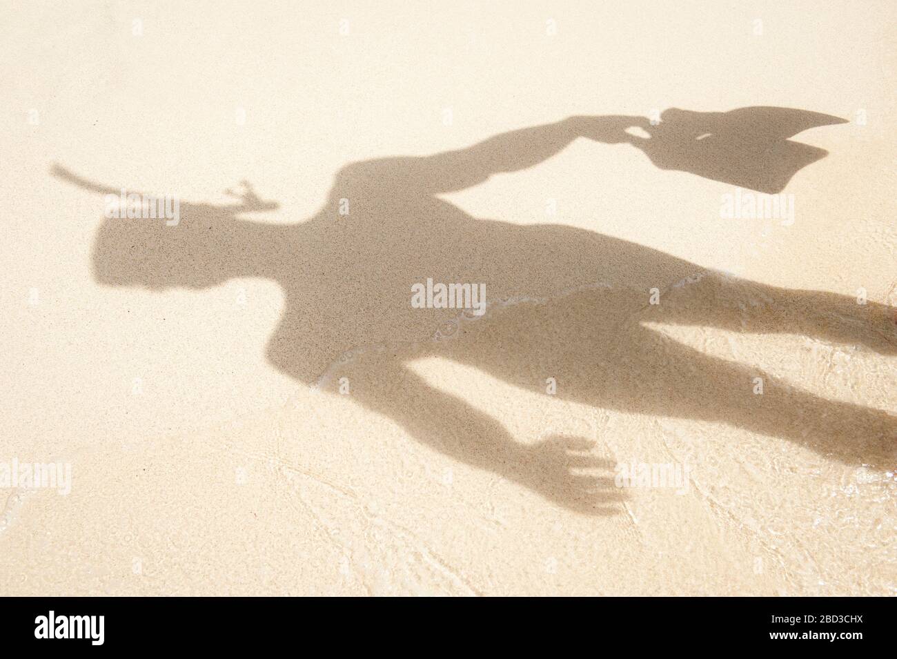 Shadow of unrecognizable snorkeler standing on a smooth tropical beach ...