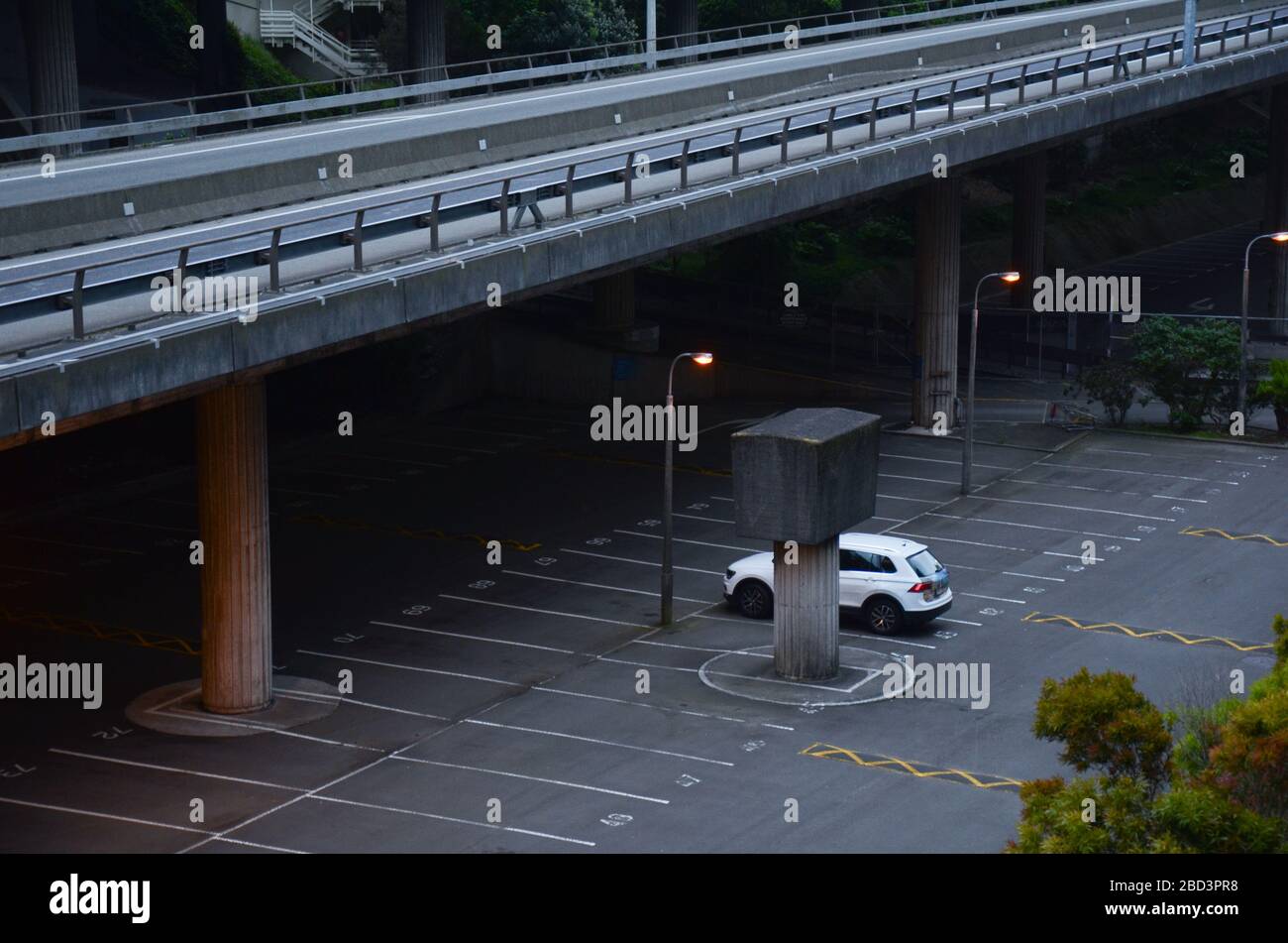 White car hiding behind concrete pole in empty parking lot with freeway ...