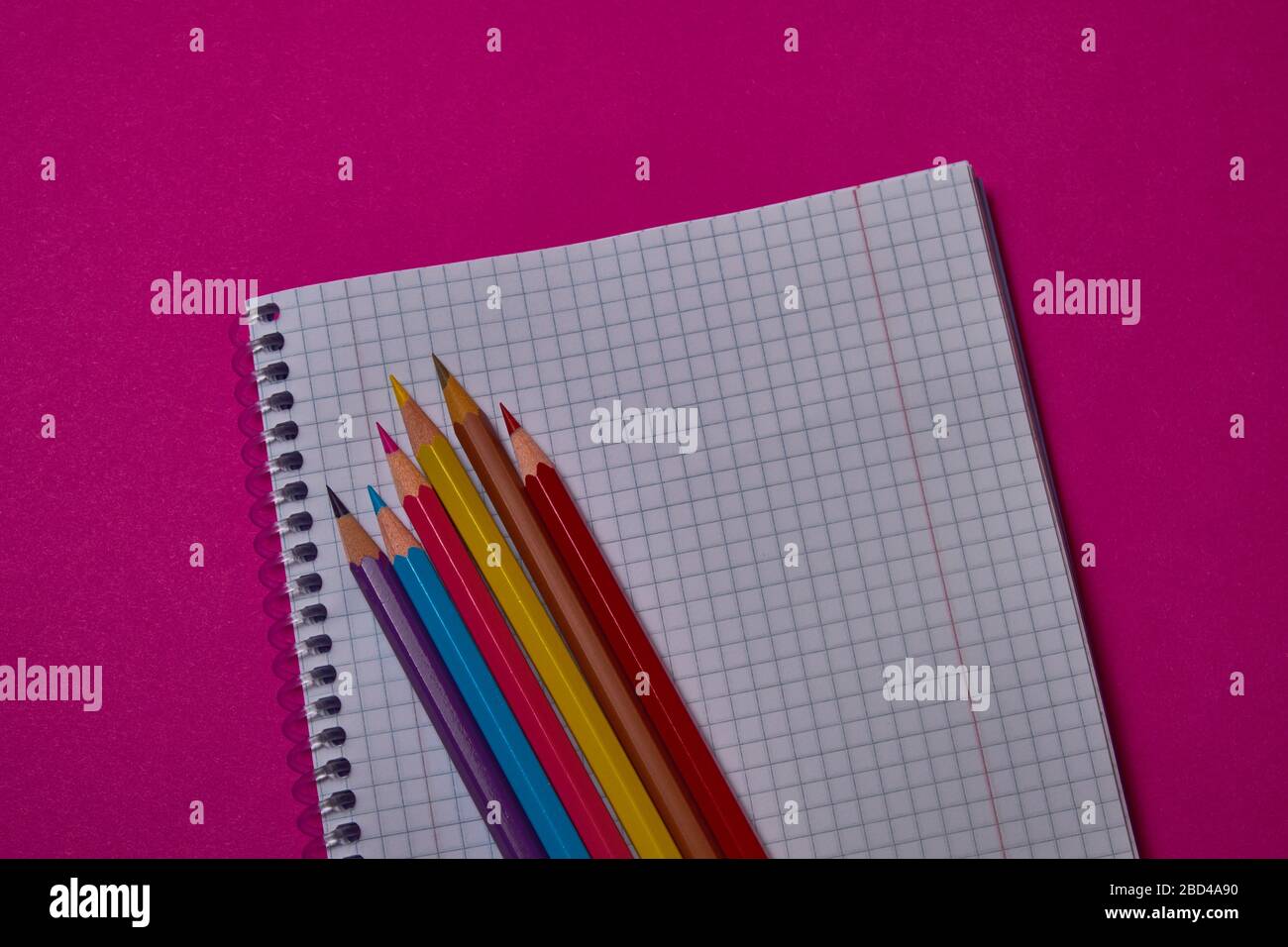 Multi colored crayons and binder notepad at magenta background with ...