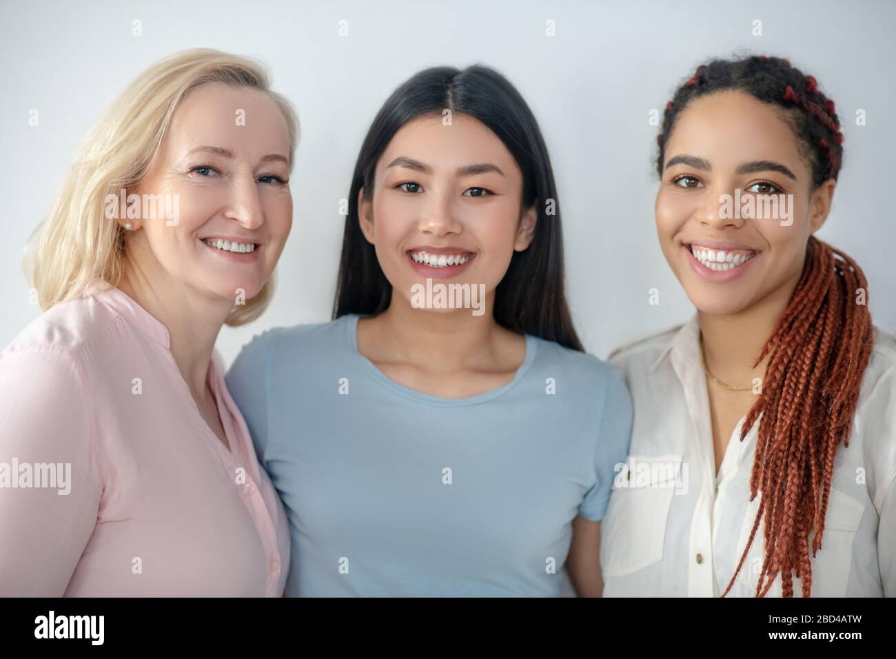 Three women standing near the wall smiling nicely Stock Photo - Alamy