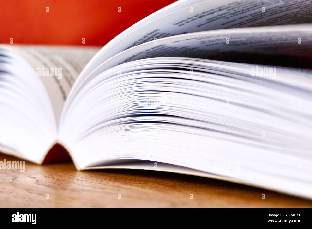 Open text book with visible pages on wooden desk against a red ...