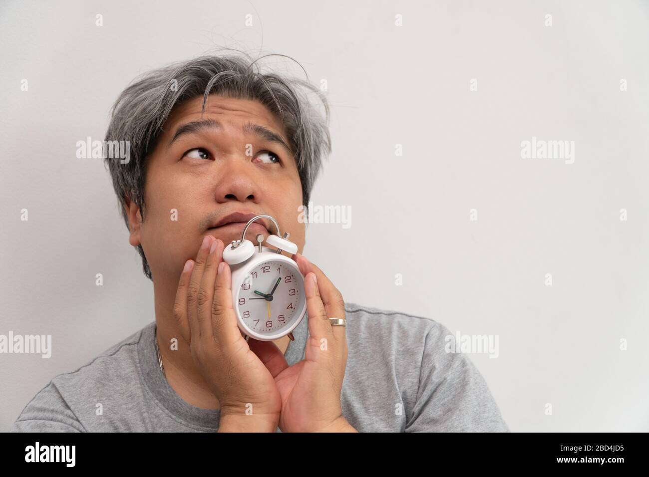 Asian middle-aged man is holding a white alarm clock and his face ...