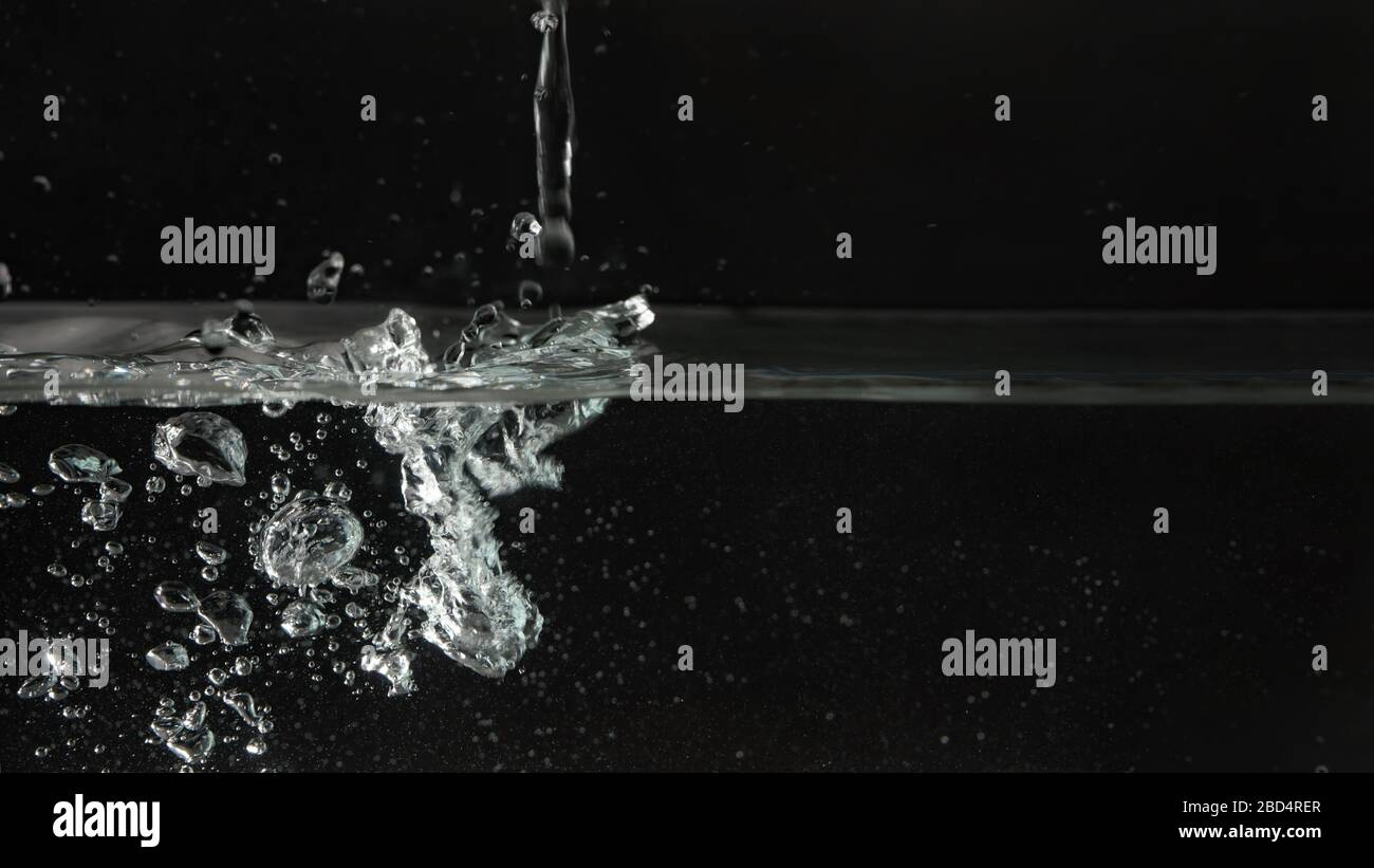 Water splashing as it's poured into aquarium tank, black background ...