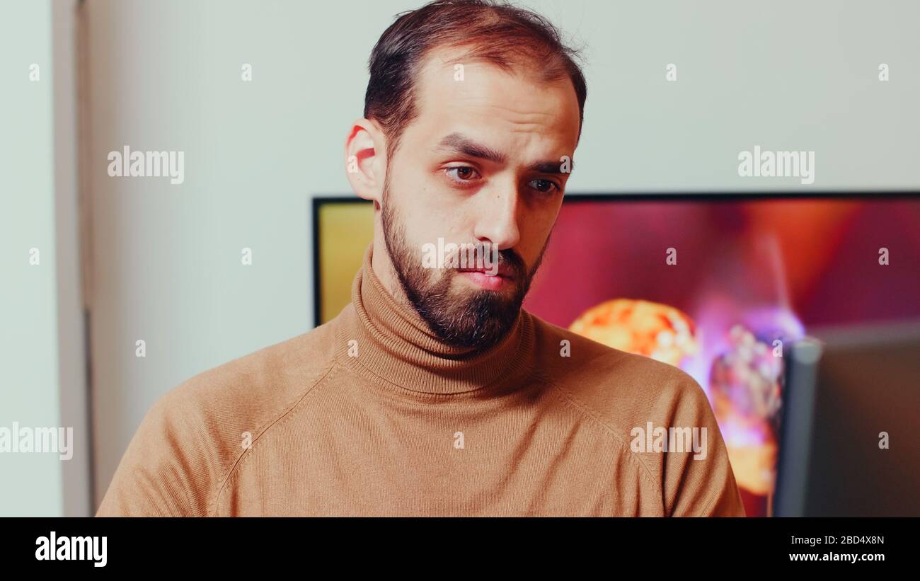 View of young game developer working on computer in home office at ...
